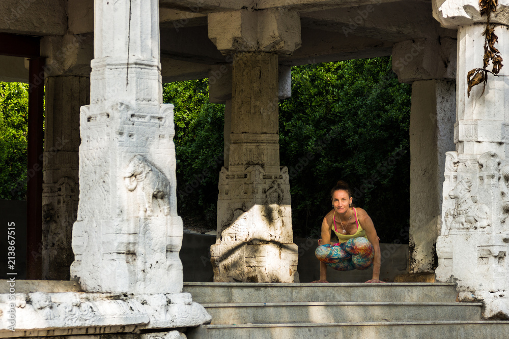 Woman practicing yoga in utpluthih pose in temple between columns with ...