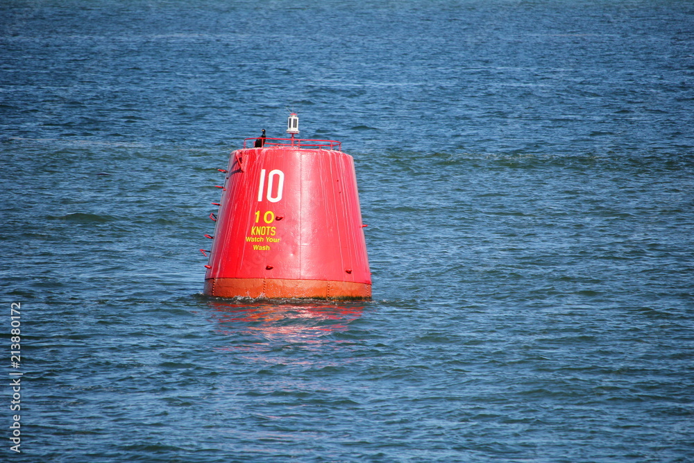 Red beacon buoy with speed limit of ten knots, floating in blue sea or ...