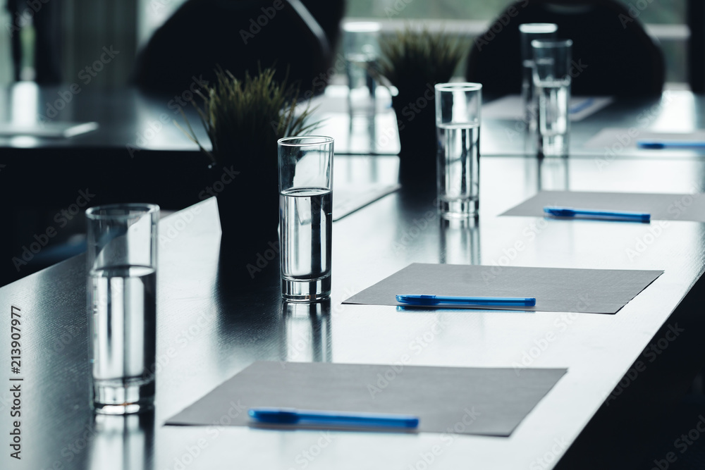 Close up of dark conference table water glasses pens, paper sheets ...