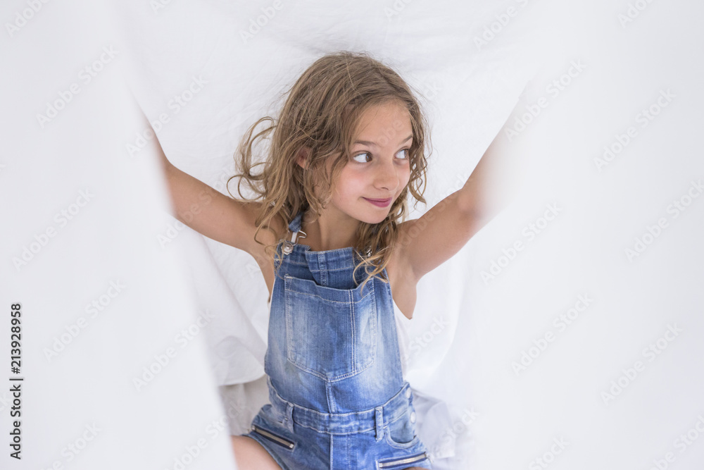 beautiful kid girl playing under white sheets on bed. Fun indoors ...