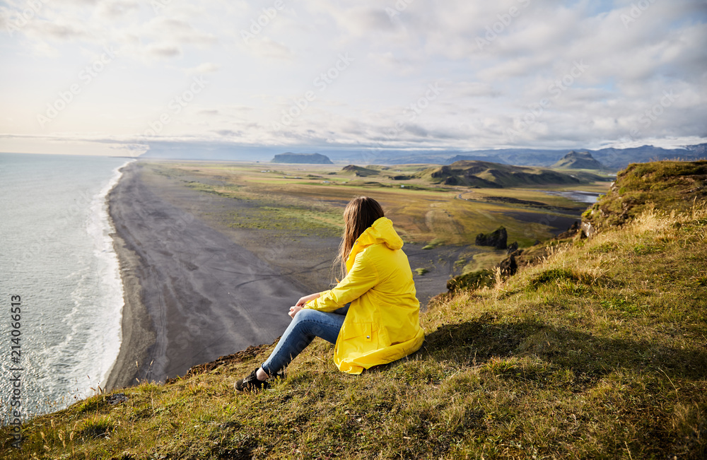 Young girl sitting on a cliff. The girl admires the sunset in Iceland ...