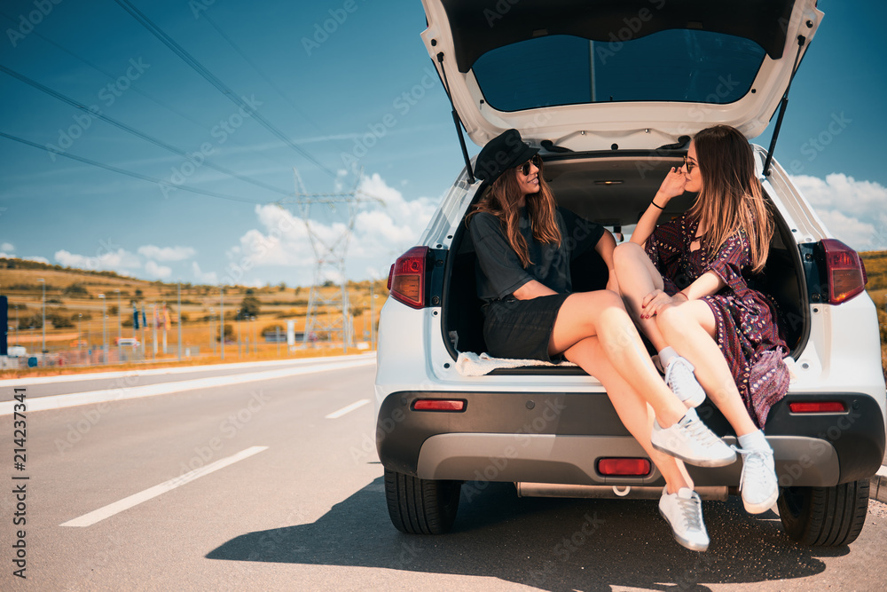 Two girls sitting in the trunk and talking. Car parked on the road ...
