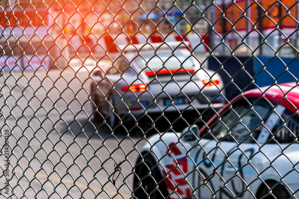 Motorsport car racing on asphalt road. View from the fence mesh netting ...