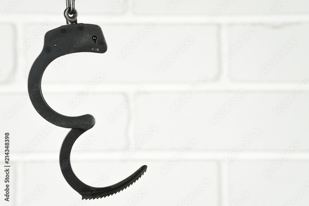 Open / unlocked police handcuffs against a white brick wall. Potential ...