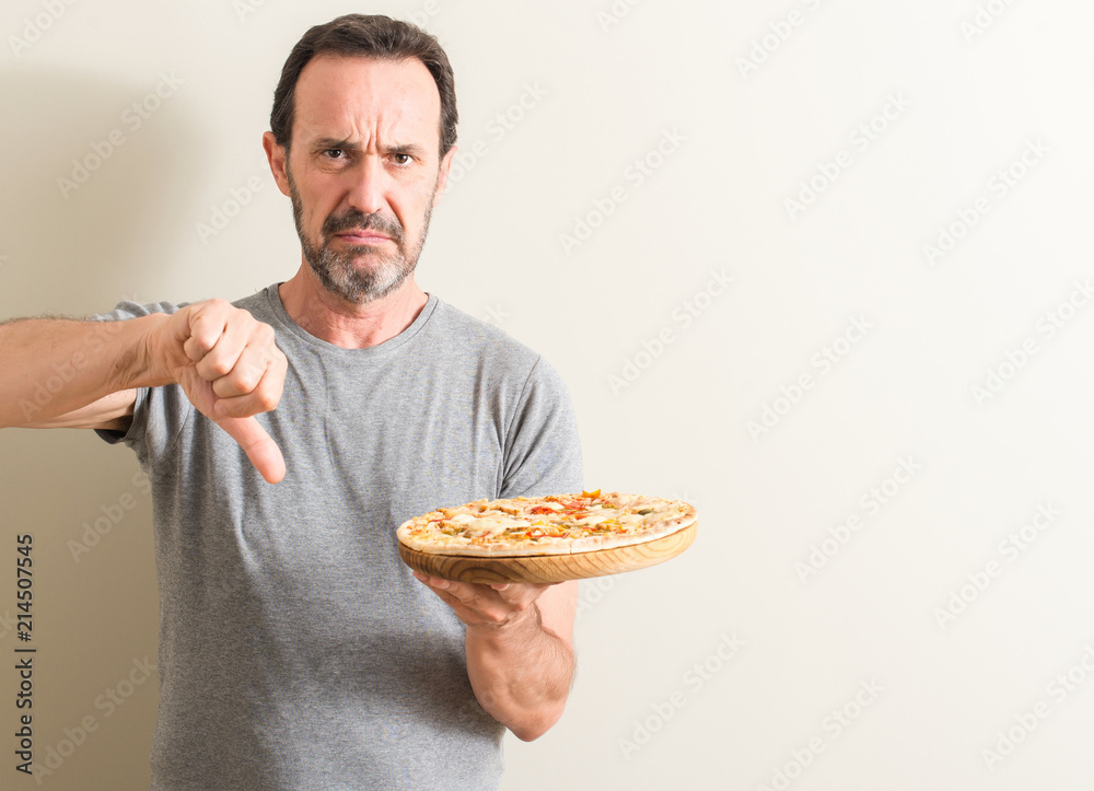 Senior man holding pizza with angry face, negative sign showing dislike ...