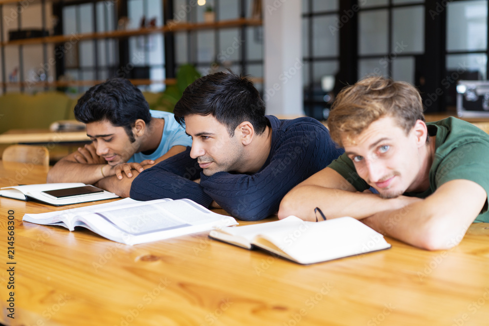Three content students resting on desk with textbooks. Young men ...