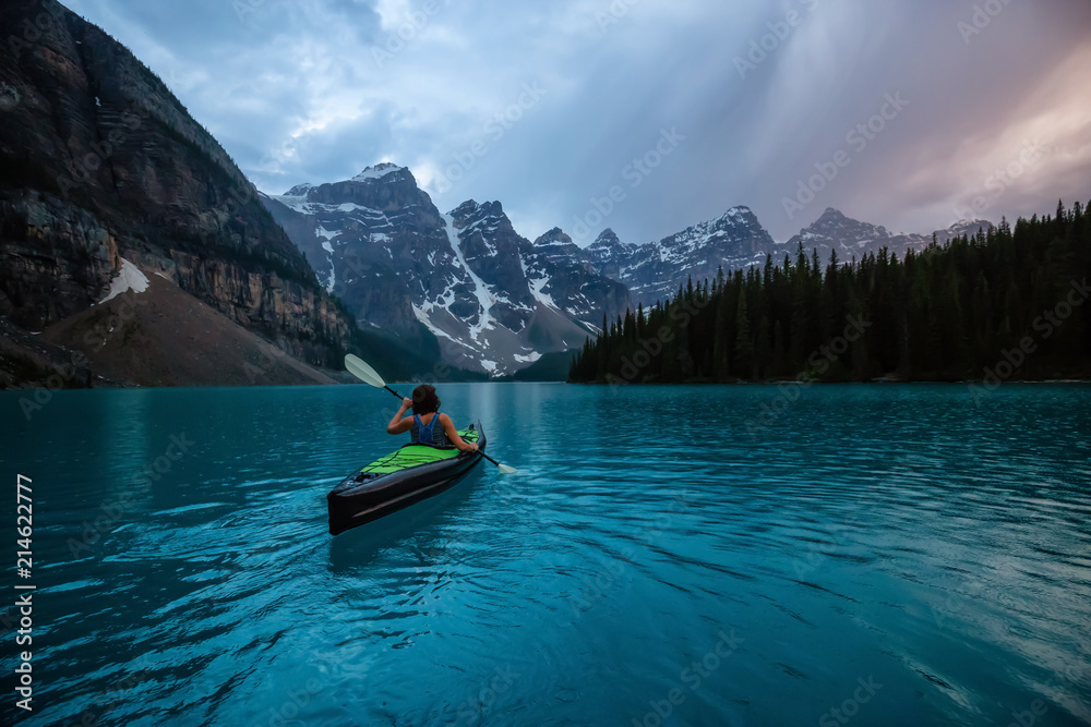 Adventurous woman kayaking in Moraine Lake during a striking cloudy ...
