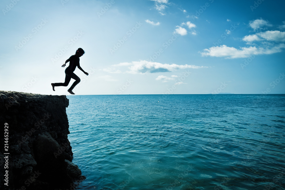 Silhouette Boy jumping off a cliff into the ocean. Boy diving into the ...