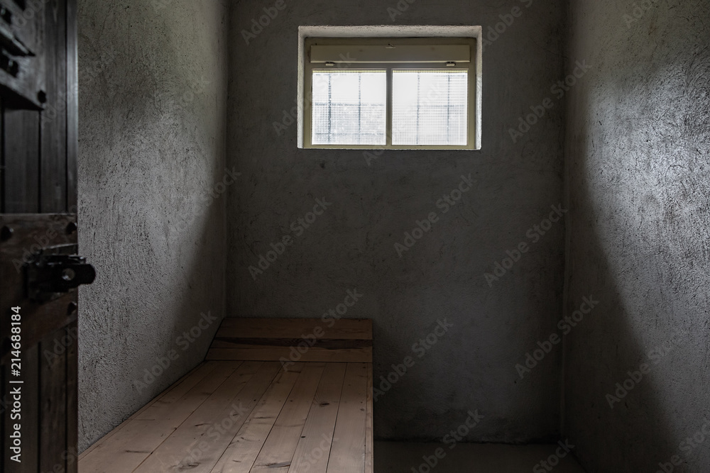 Small prison concrete cell with one small window and one wooden pallet ...