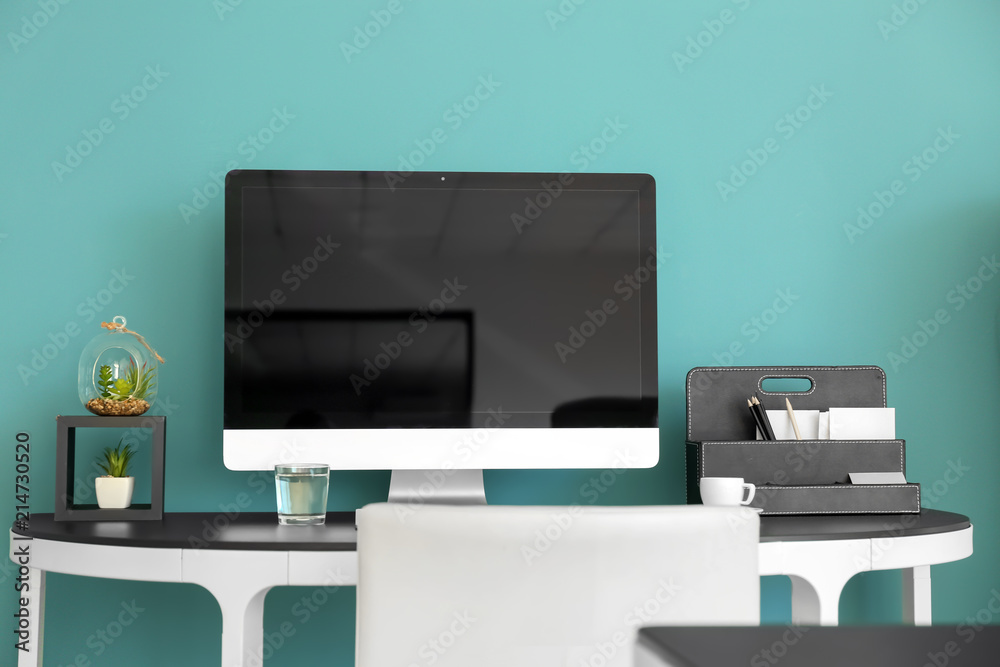 Stylish workplace with computer on table near color wall in office ...