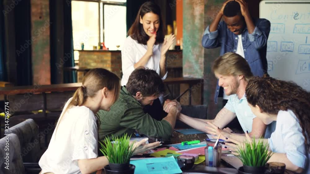 Joyful male colleagues are practicing arm wrestling at workplace then ...