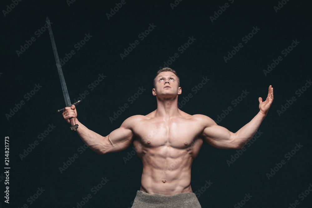 Bodybuilder man posing with a sword isolated on black background ...