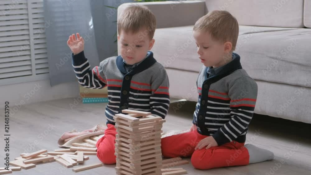 Twins boys brothers are building a tower from wooden blocks sitting on ...