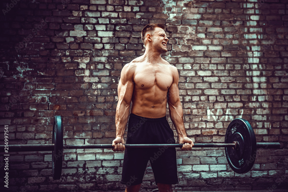 Athletic man working out with a barbell in front of brick wall ...