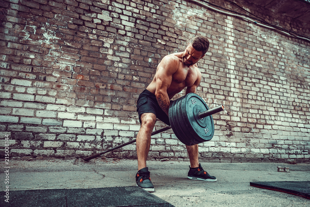Athletic man working out with a barbell in front of brick wall ...