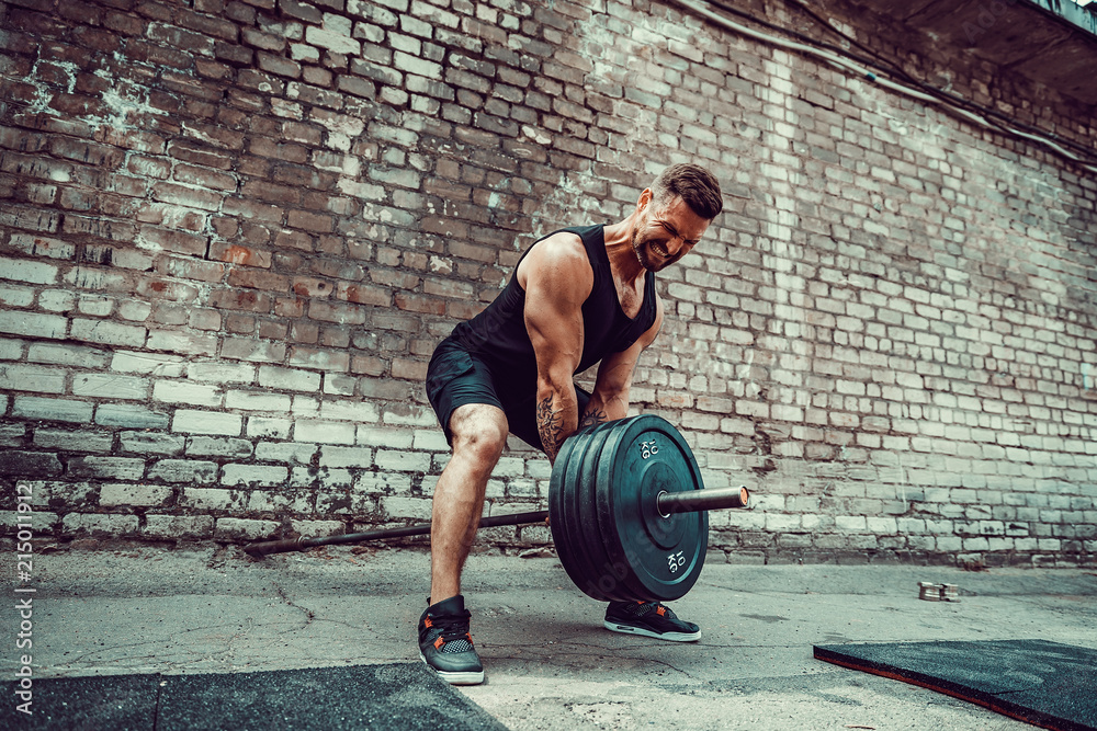 Athletic man working out with a barbell in front of brick wall ...