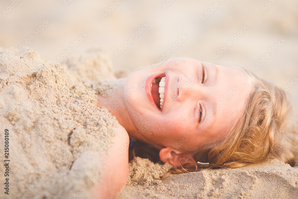 Close up of laughing young girl covered with sand lying on the beach ...