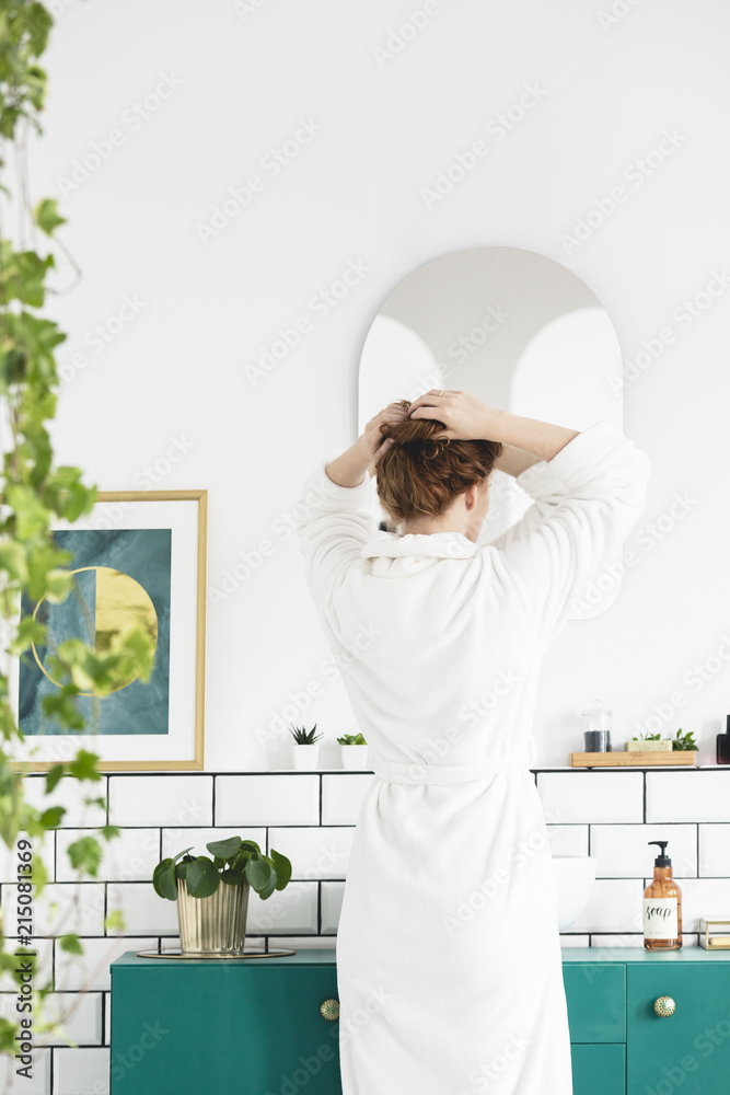 Woman in white dressing-gown in front of mirror in bathroom interior ...