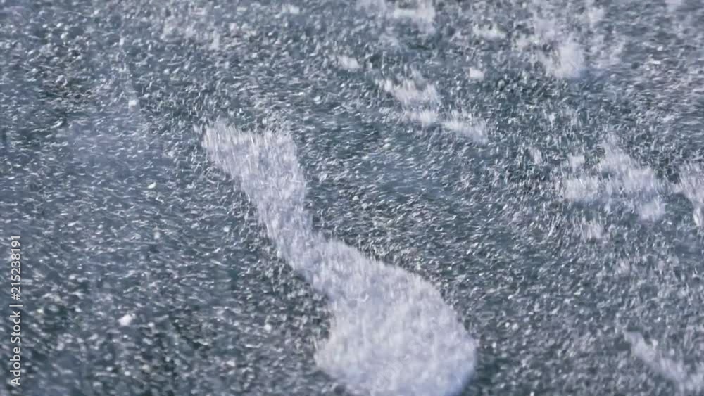Snow is flying over surface of ice. Snowflakes fly on ice of Lake ...