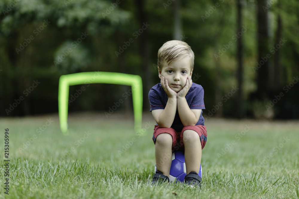 Cute young boy sitting on a soccer ball Stock Photo | Adobe Stock