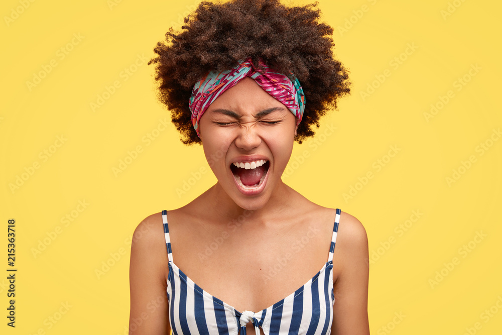 Furious attractive curly young female with dark skin, opens mouth as ...