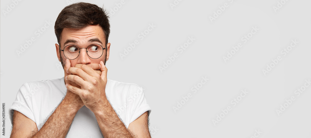 Scared anxious young male has eyes popped put, looks with fear aside ...