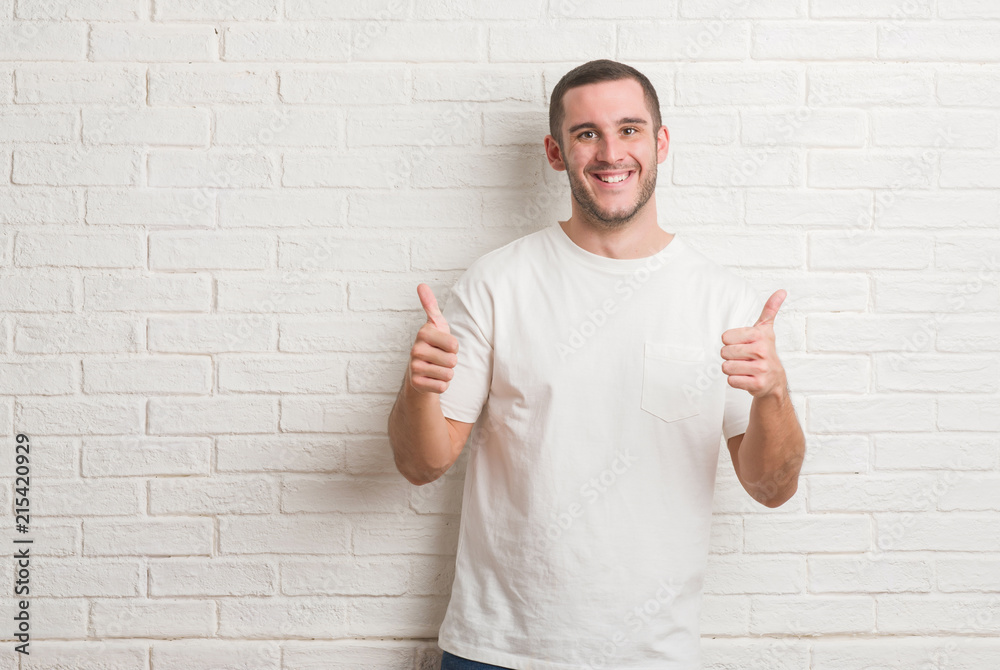 Young caucasian man standing over white brick wall disgusted expression ...