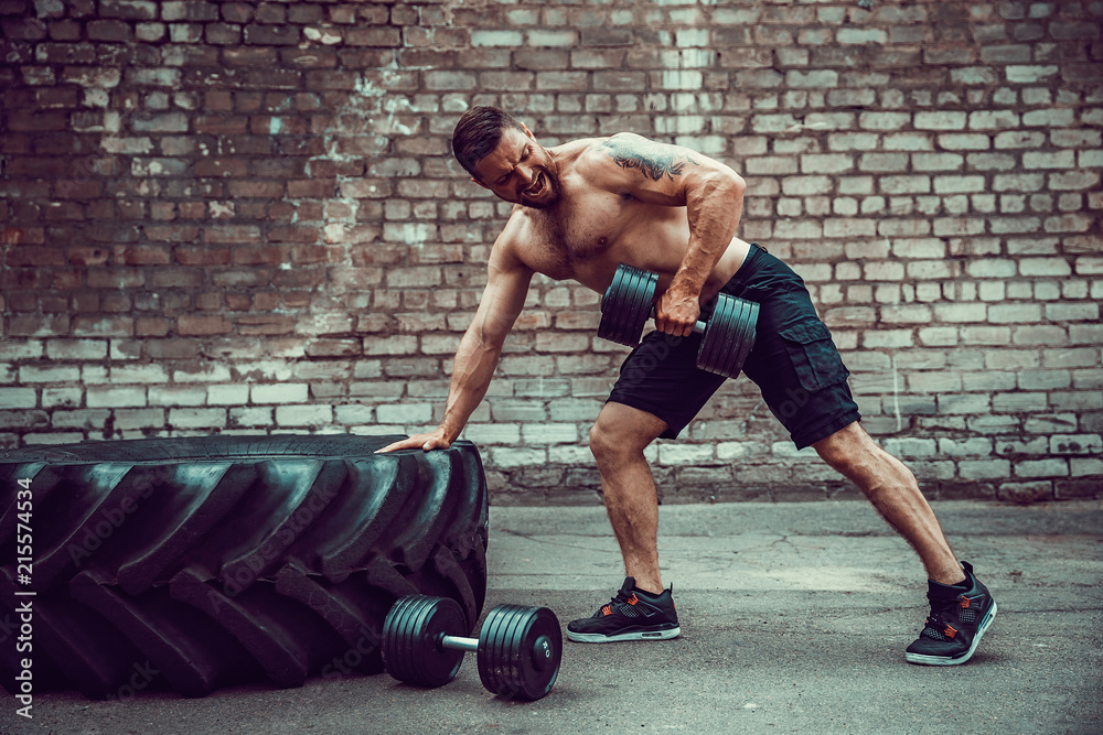 Athletic man working out with a dumbbell in front of brick wall ...