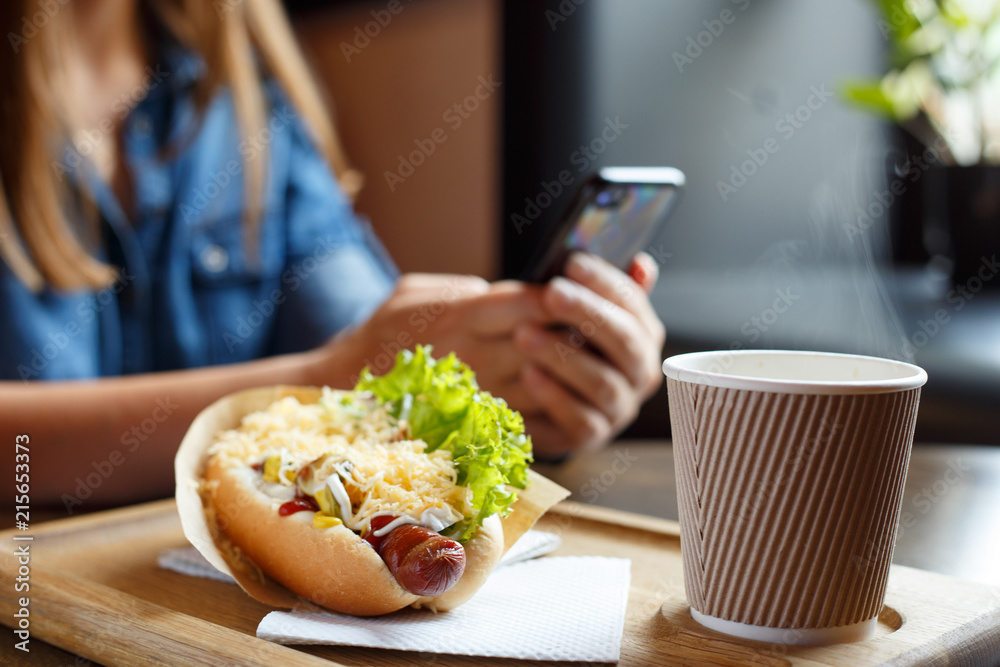 Lunch concept background. Young woman at meal time in cafe with hot dog ...