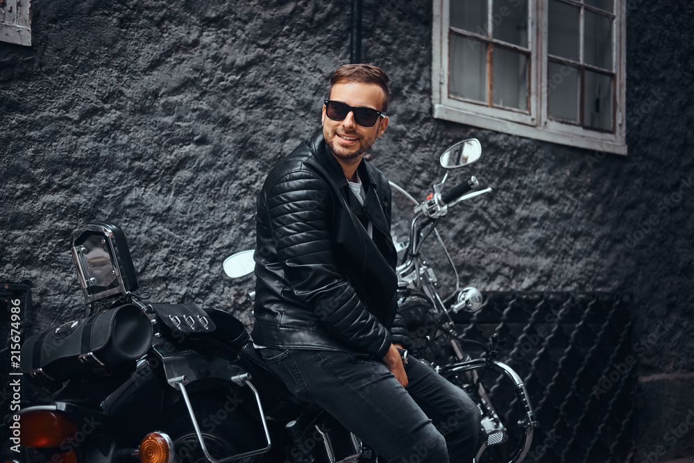 Fashionable biker dressed in a black leather jacket and jeans sitting ...