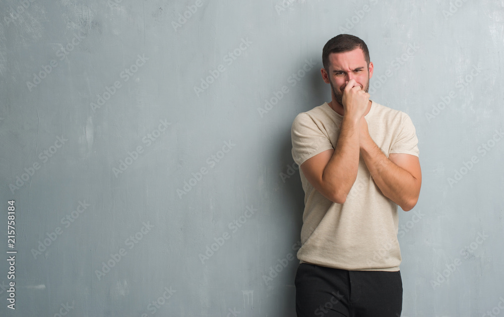 Young caucasian man over grey grunge wall smelling something stinky and ...