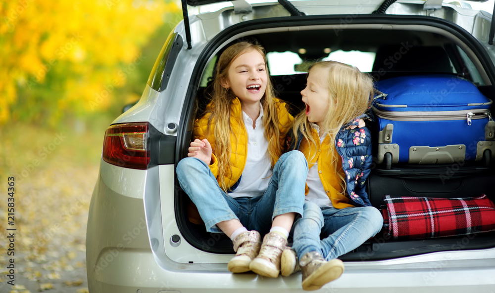 Two adorable girls sitting in a car trunk before going on vacations ...