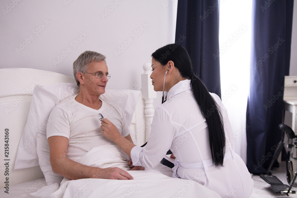 Aged man with grey hair and glasses laying in bed being checked up by ...