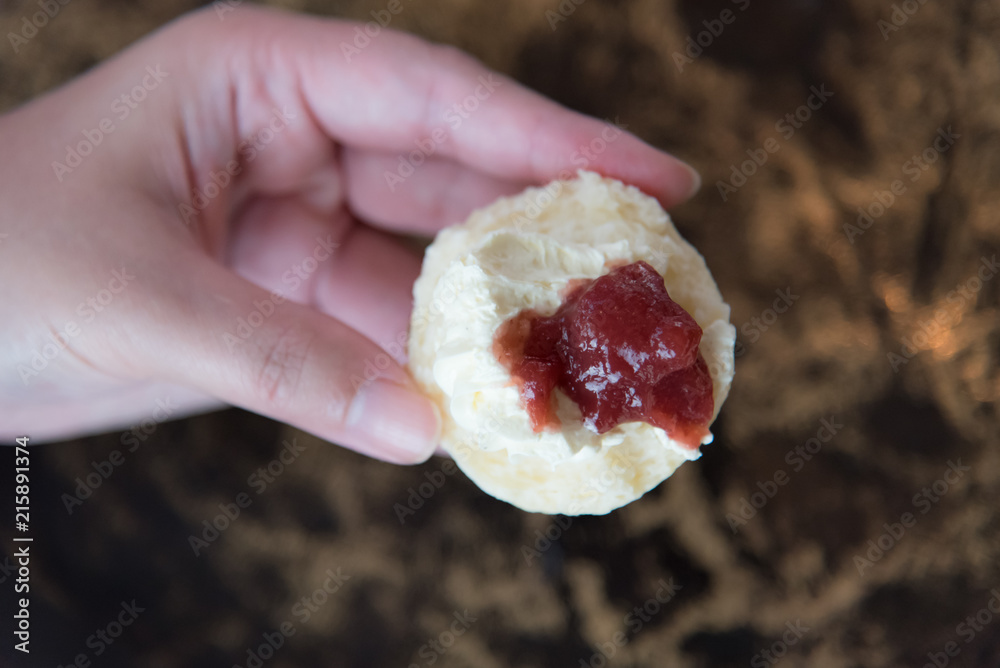 Hand of Asian woman hold a half split freshly baked scone spread with ...