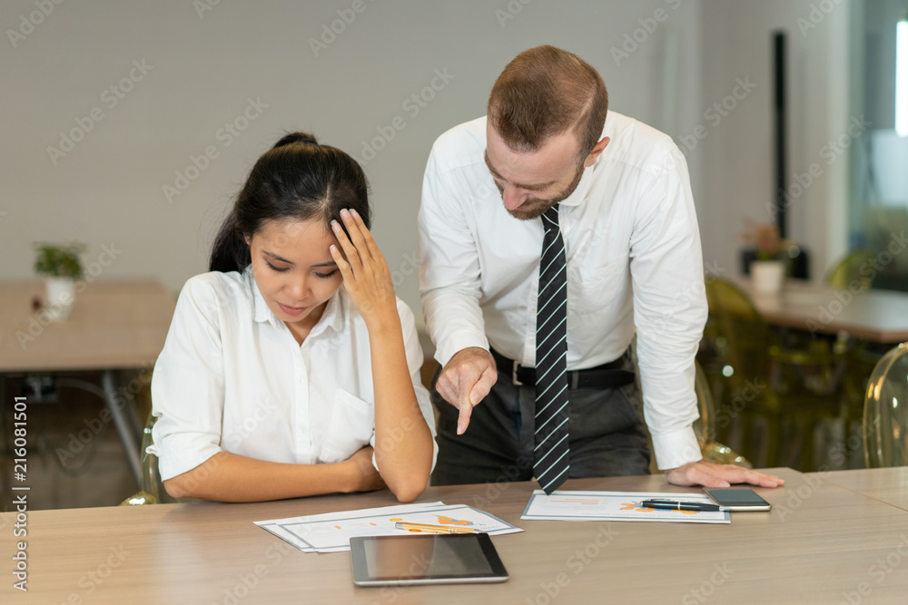 Angry boss pointing at report while berating Asian employee. Annoyed ...