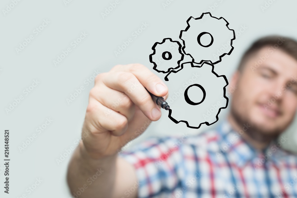 Man with black marker draws on a transparent board or glass wall. Gear ...