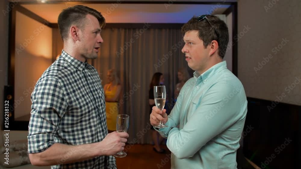 Two Male friends drinking champagne and chatting in the apartment party ...