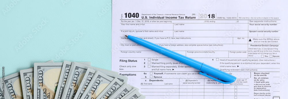 1040 tax form lies near hundred dollar bills and blue pen on a light ...