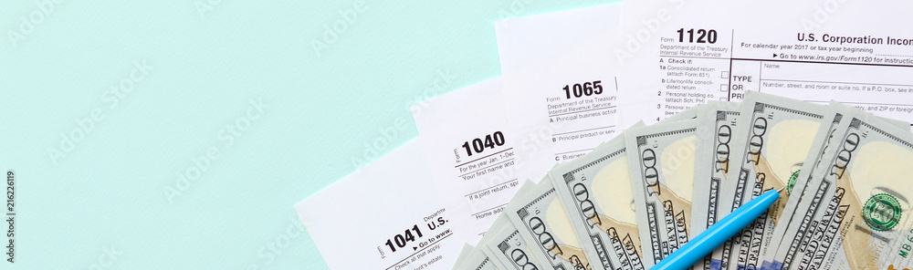 Tax forms lies near hundred dollar bills and blue pen on a light blue ...