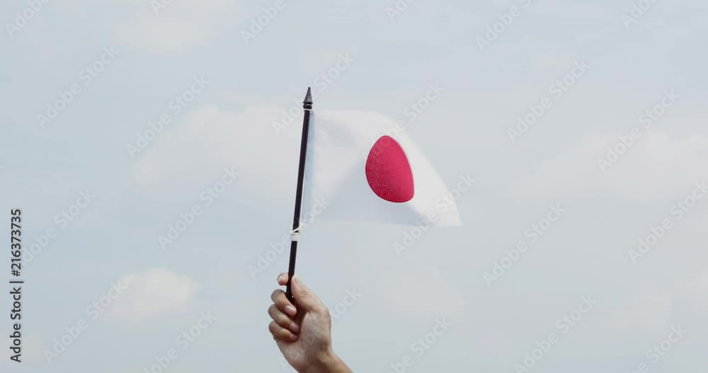 Hand raising national flag of Japan under clear sky with white clouds ...