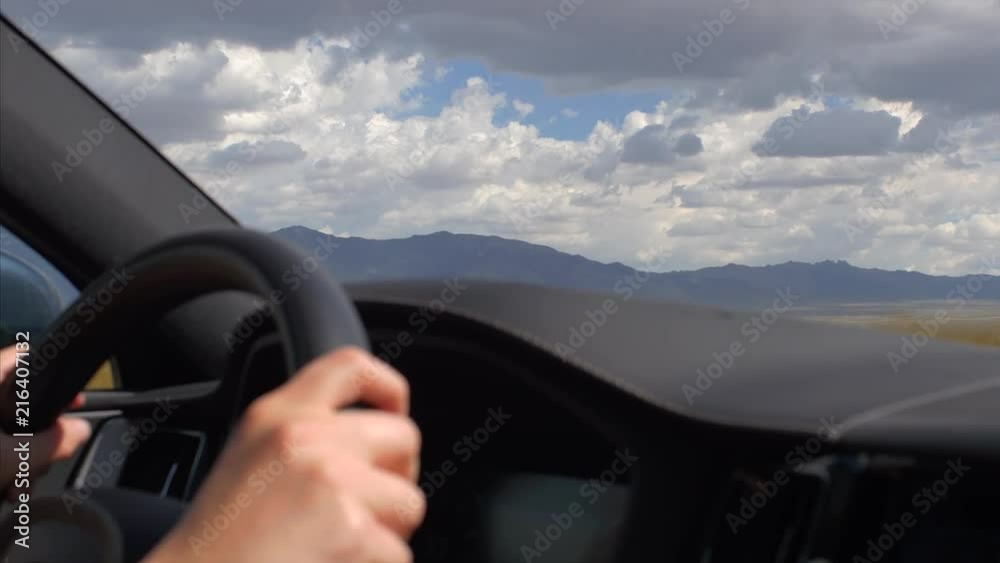 Holding on to a steering wheel, driving through the desert on a road ...