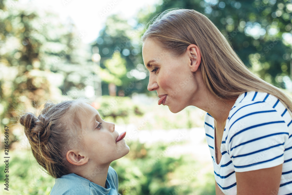 Profile of happy mother and daughter showing tongues to each other with ...
