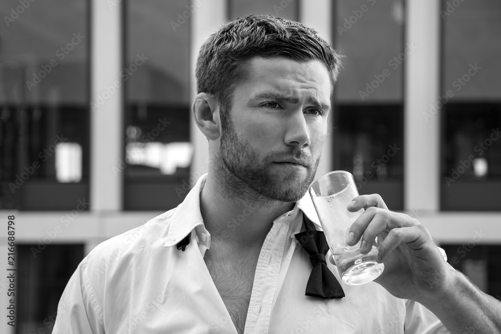 Handsome hunky man in tuxedo, unbuttoned shirt and tie stands on hotel ...