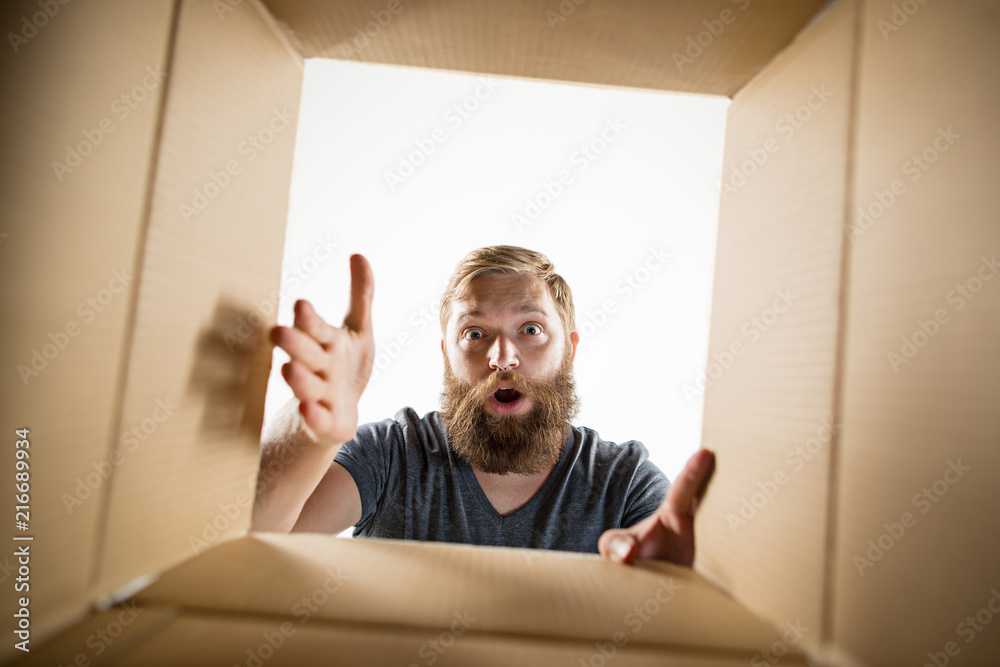 The surprised man unpacking, opening carton box and looking inside. The ...