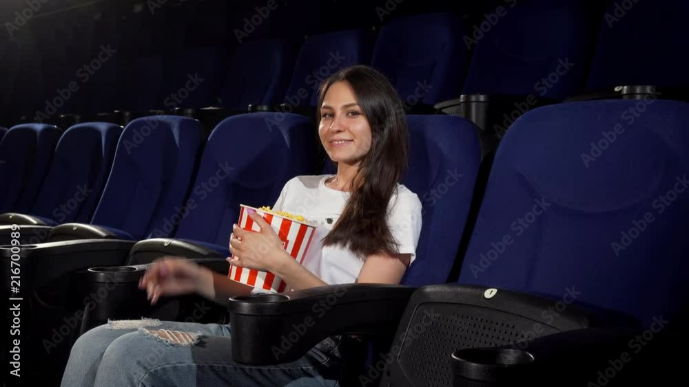 Young attractive woman pointing at the seat beside her at the movie ...
