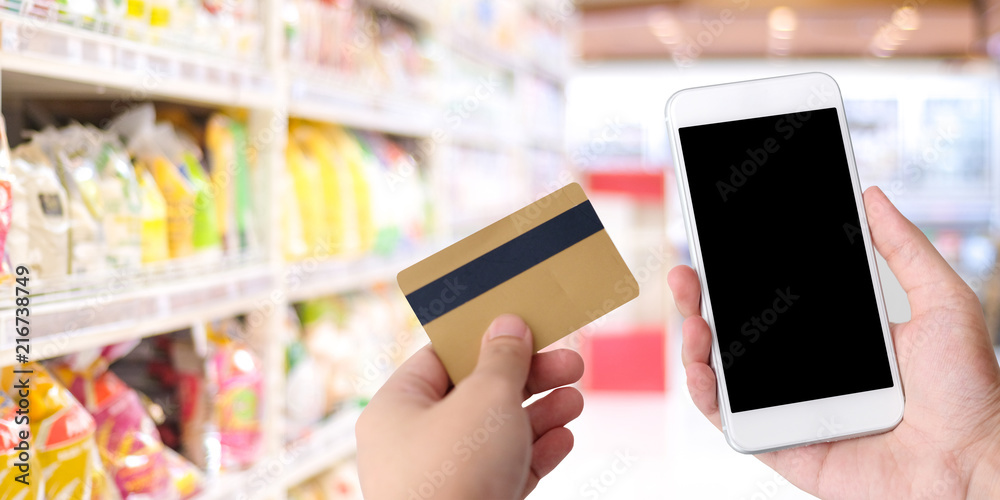 Hand holding credit card and smart phone with blank screen over blur ...