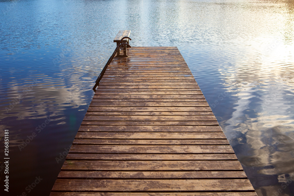 Beautiful wooden pier with clouds and sun reflected on calm and blue ...