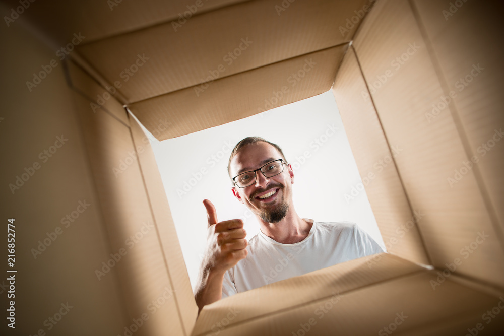 The surprised man unpacking, opening carton box and looking inside. The ...