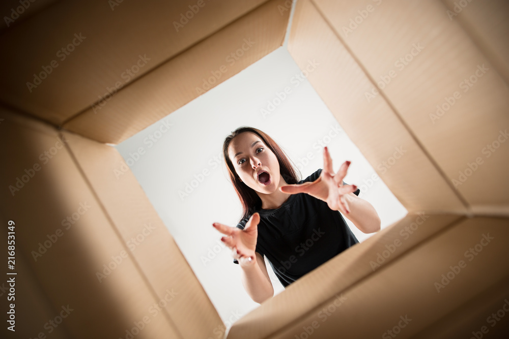 The surprised woman unpacking, opening carton box and looking inside ...