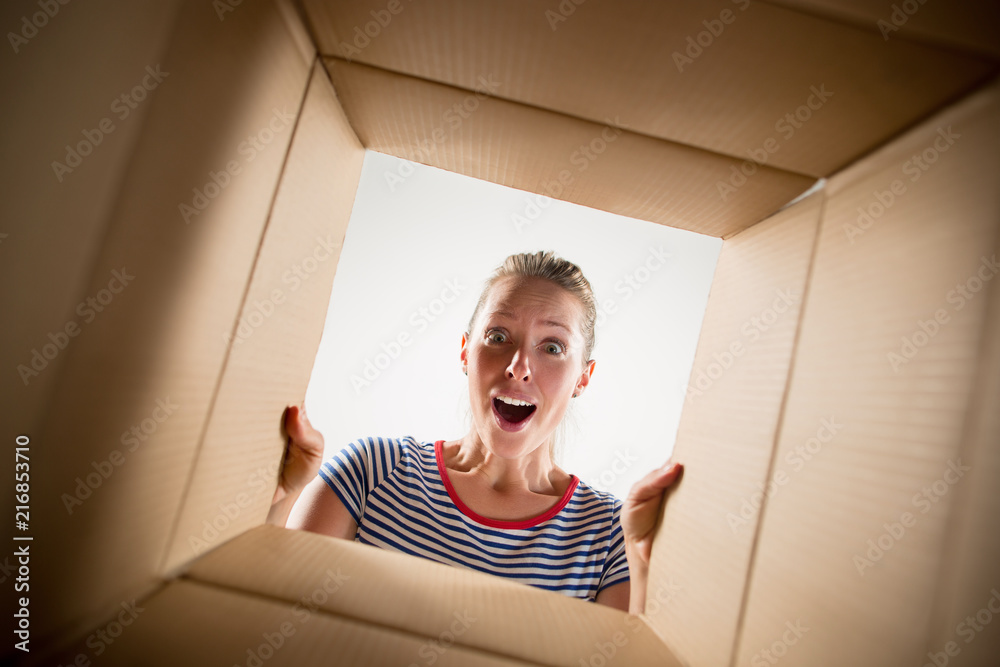 The surprised woman unpacking, opening carton box and looking inside ...